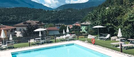 Piscina com espreguiçadeiras e guarda-sóis, cercada por montanhas e vegetação.