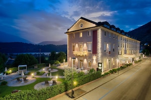 Um hotel com fachada bem iluminada, um jardim paisagístico com assentos e vista para a paisagem ao redor.