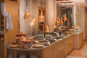 Um buffet de café da manhã com diversos pães, pratos e salgados, armários de madeira e luminárias pendentes.