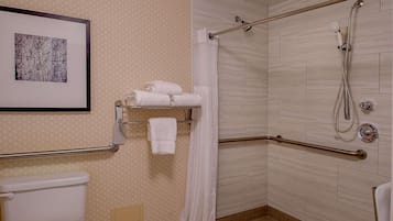 Um banheiro com vaso sanitário, chuveiro com barra de apoio, porta-toalhas com toalhas e um quadro na parede.