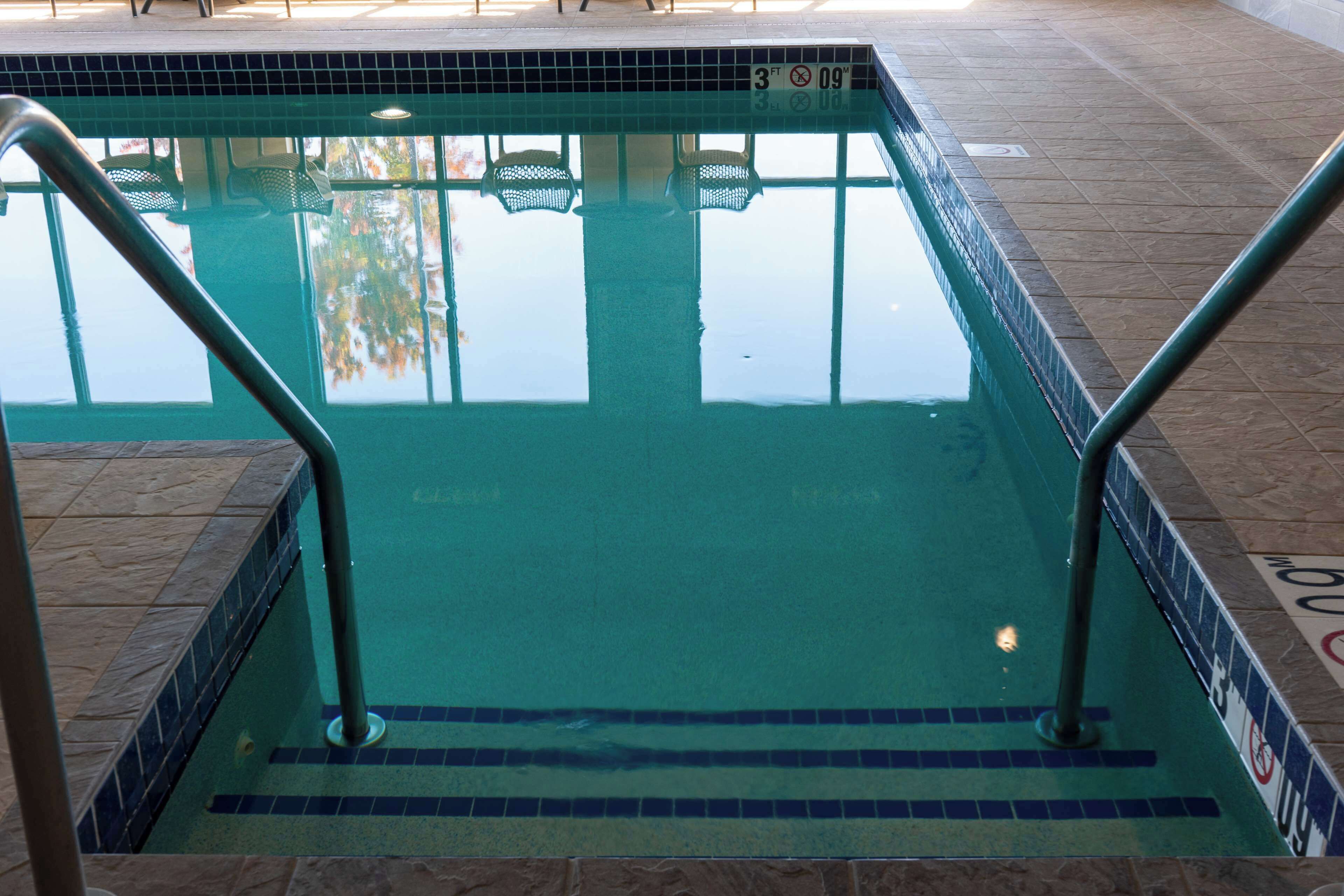 Piscina com água cristalina, bordas azulejadas e corrimãos de metal.