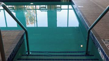 Piscina com água cristalina, bordas azulejadas e corrimãos de metal.