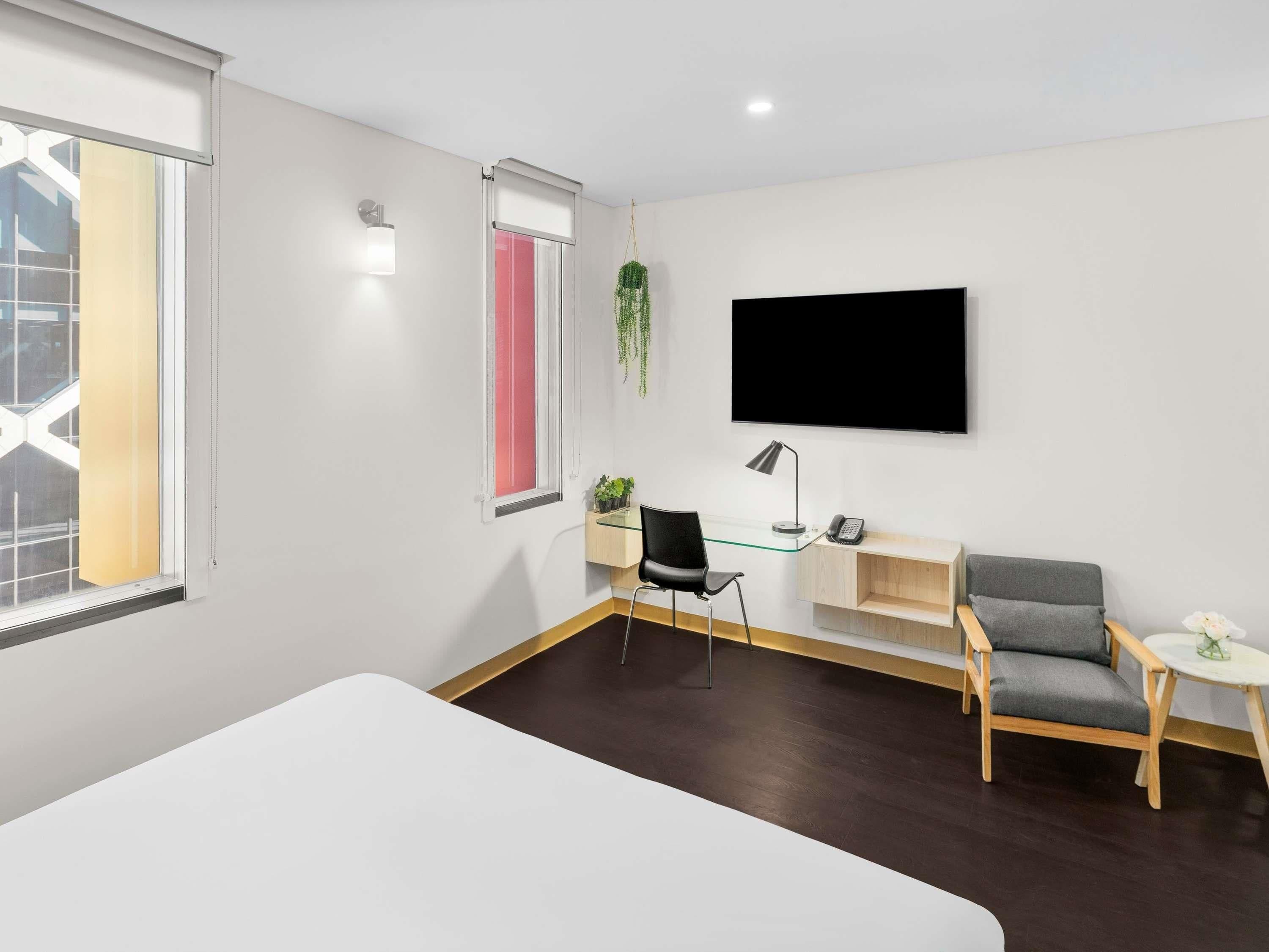 Quarto de hotel moderno com cama, escrivaninha, cadeira e televisão de tela plana na parede.