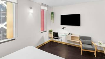 Quarto de hotel moderno com cama, escrivaninha, cadeira e televisão de tela plana na parede.