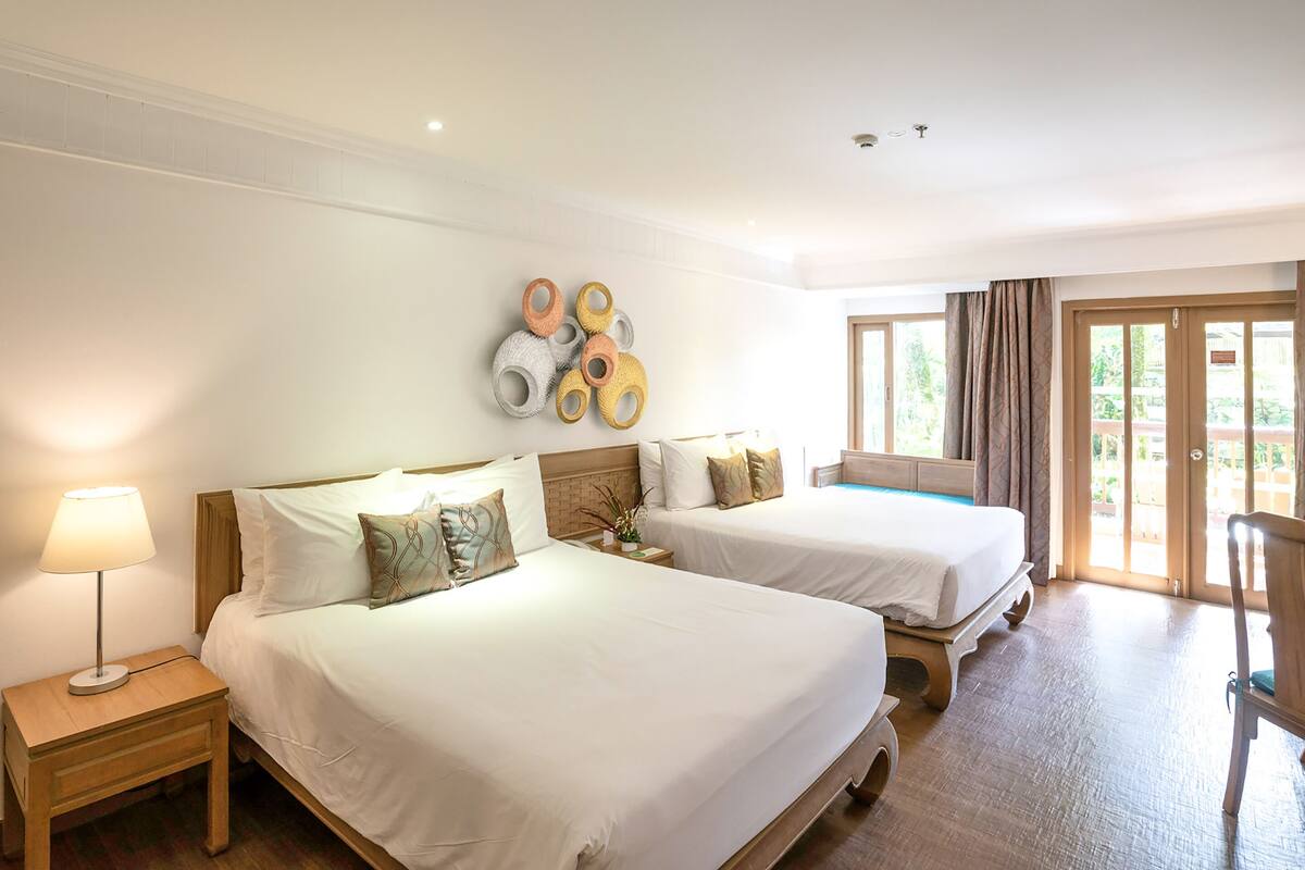 Quarto de hotel com duas camas, mesa de cabeceira, abajur, um objeto decorativo na parede e vista para o exterior.