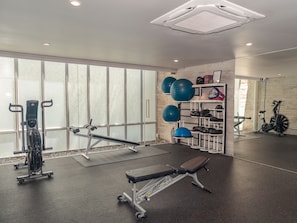 Academia com equipamentos de ginástica, um banco e uma parede com prateleiras contendo objetos.