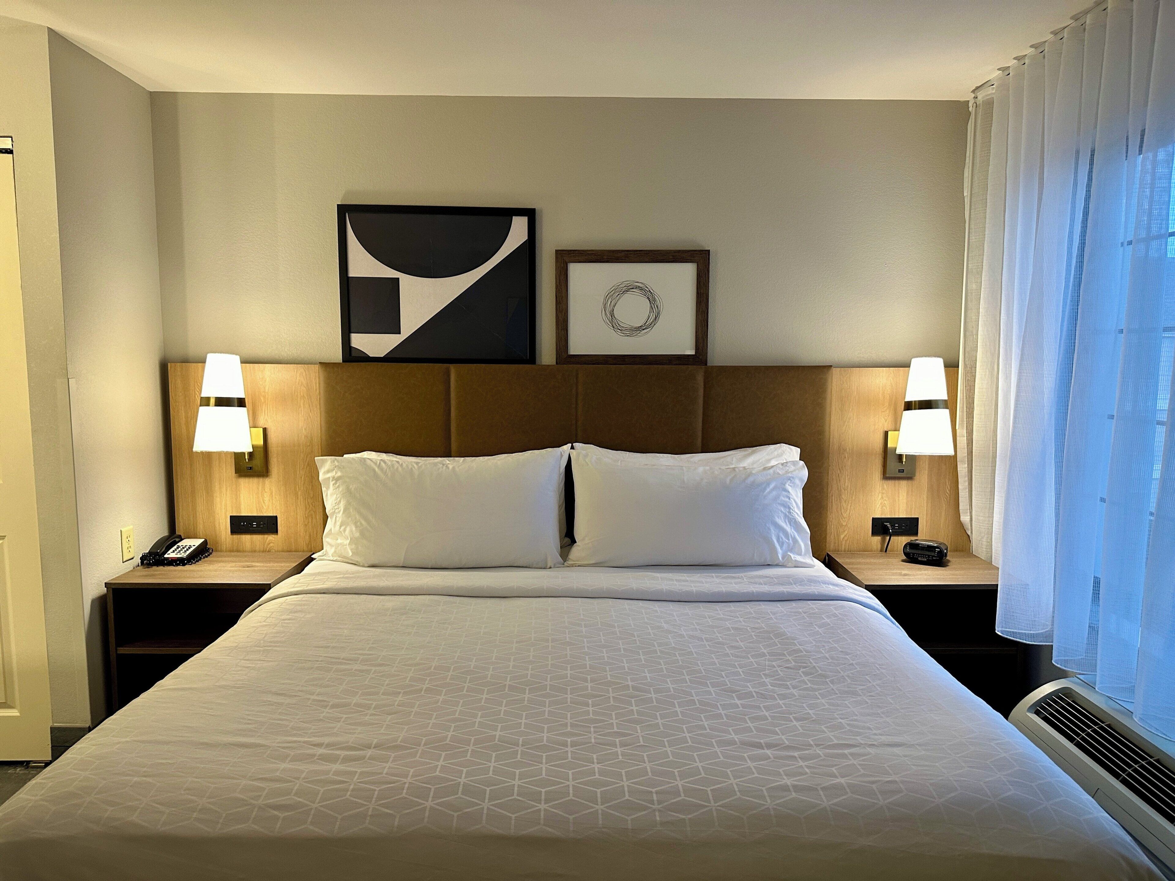 Quarto de hotel com cama grande, duas luminárias de cabeceira, telefone e quadro na parede.