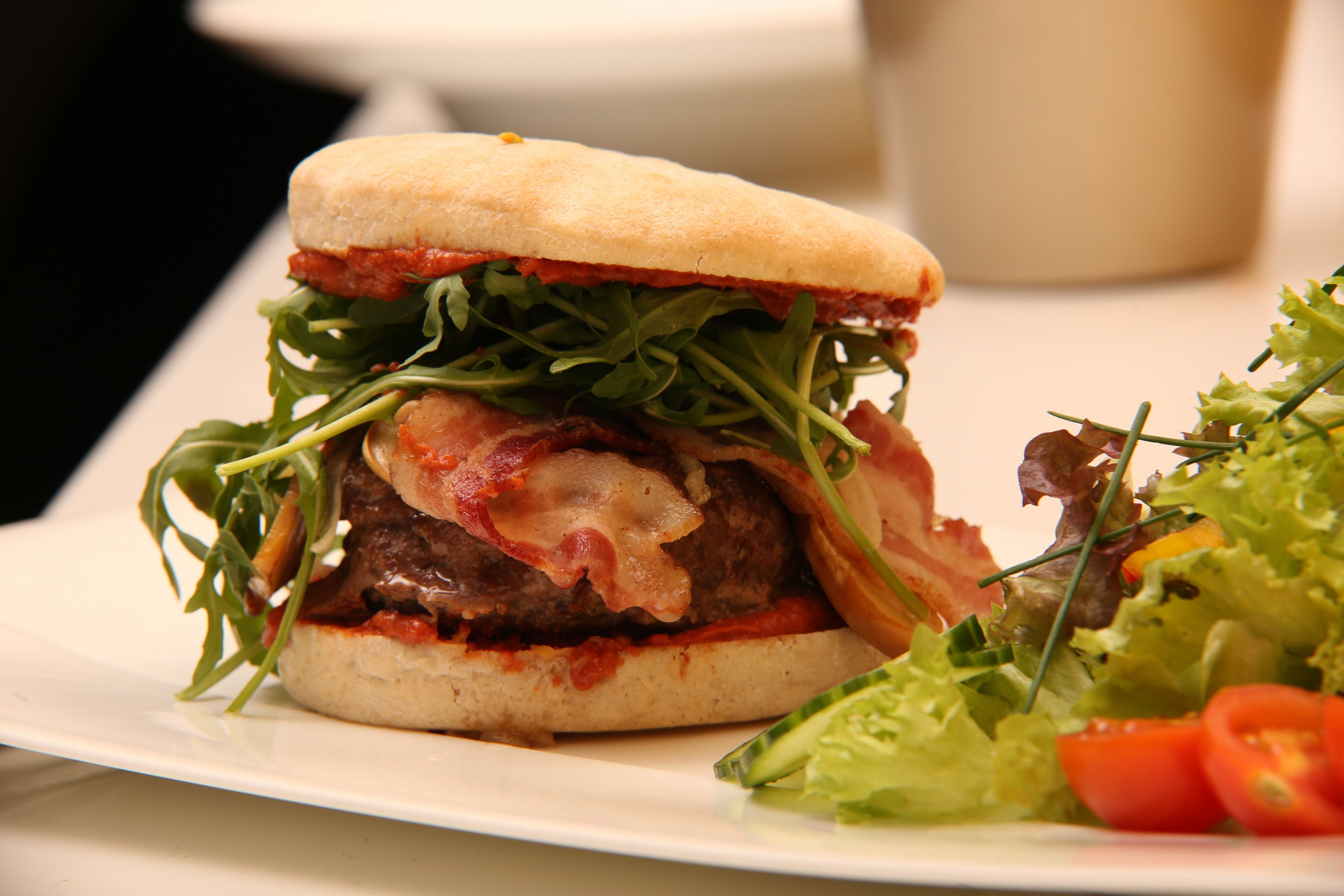 Sanduíche com alface, tomate e bacon sobre um prato branco.