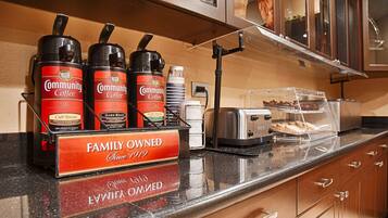 Uma estação de café com vários dispensadores, uma torradeira e uma vitrine com doces.