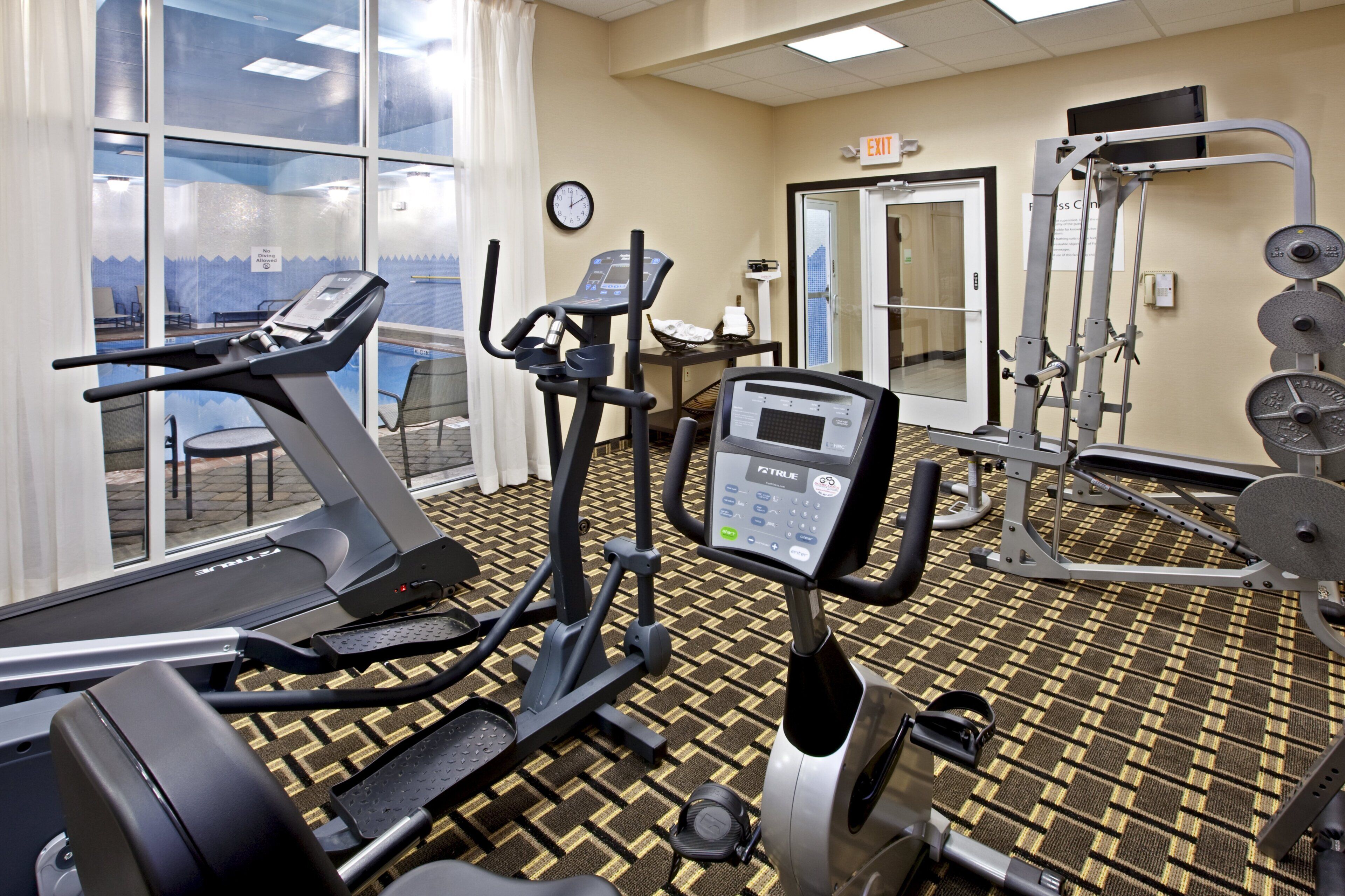 Centro de fitness com máquinas de cardio, equipamentos de peso e vista para uma piscina.