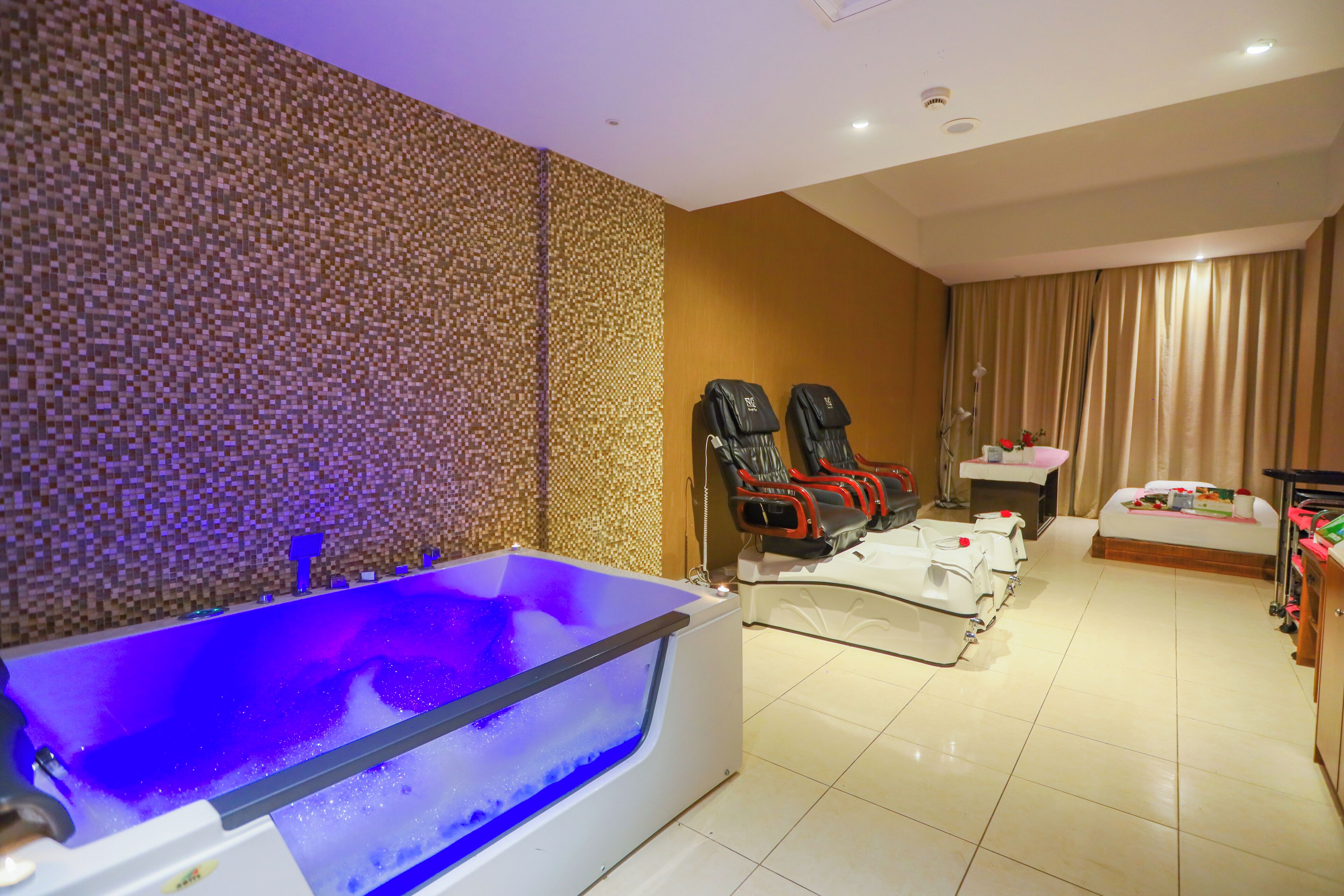 Um quarto de spa com uma banheira grande, cadeiras de massagem e uma pequena mesa com abajur.