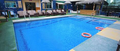 Piscina com espreguiçadeiras e guarda-sóis, placa indicando academia e área de bar.