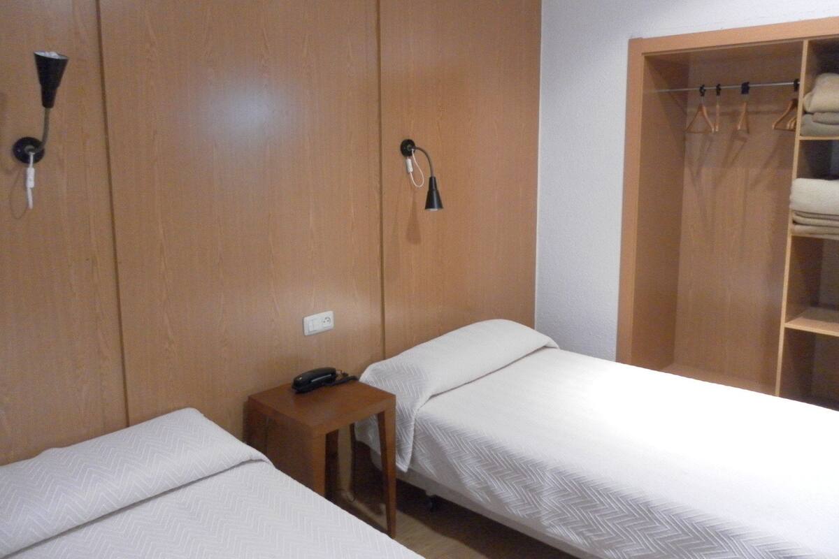 Quarto com duas camas de solteiro, guarda-roupa de madeira e uma pequena mesa de cabeceira com um telefone.