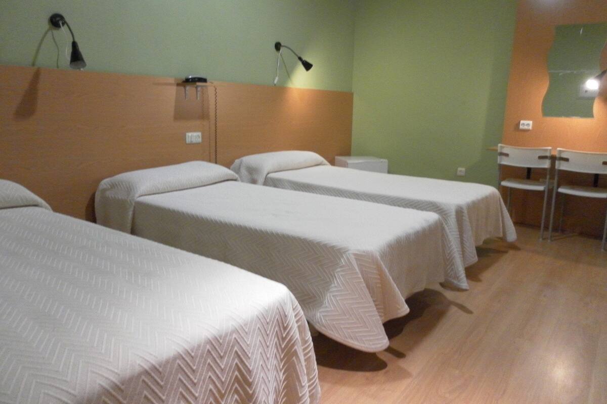 Quarto com três camas de solteiro, uma escrivaninha e duas cadeiras.