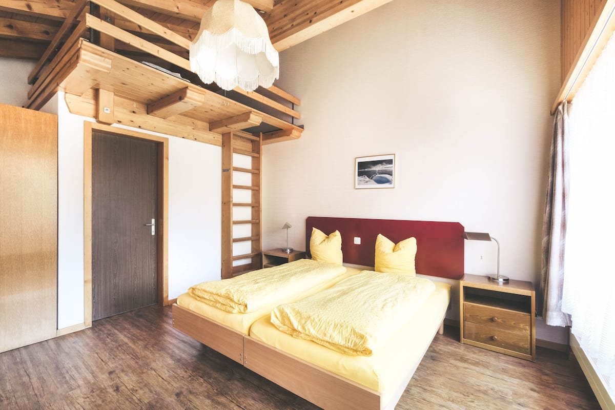Quarto com cama de madeira, escada, mesa de cabeceira e cabeceira vermelha.
