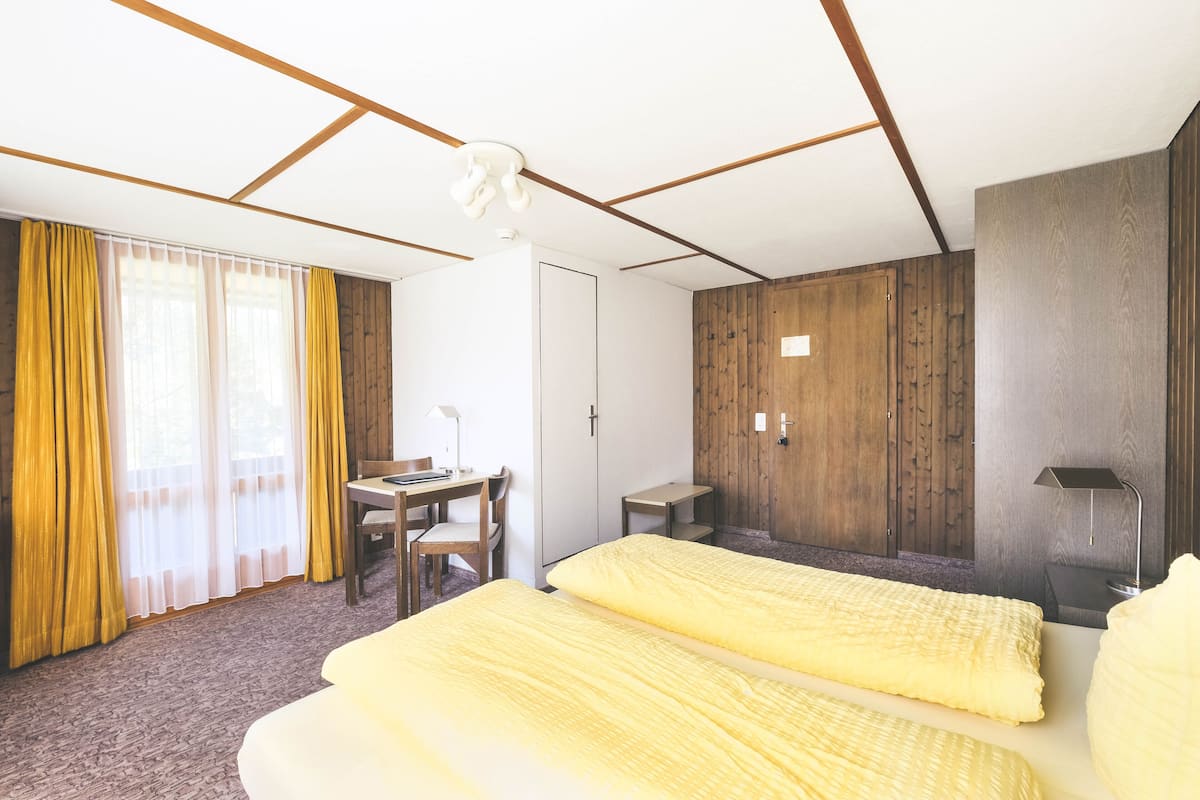 Quarto de hotel com duas camas, uma escrivaninha, uma cadeira e um guarda-roupa.