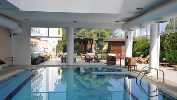 Piscina interior com água azul cristalina, rodeada por espreguiçadeiras e mesas.