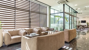 Um lobby moderno com um amplo sofá bege, uma mesa de centro e um painel de vidro.
