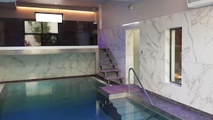 Piscina interna com paredes de mármore e barreira de vidro.
