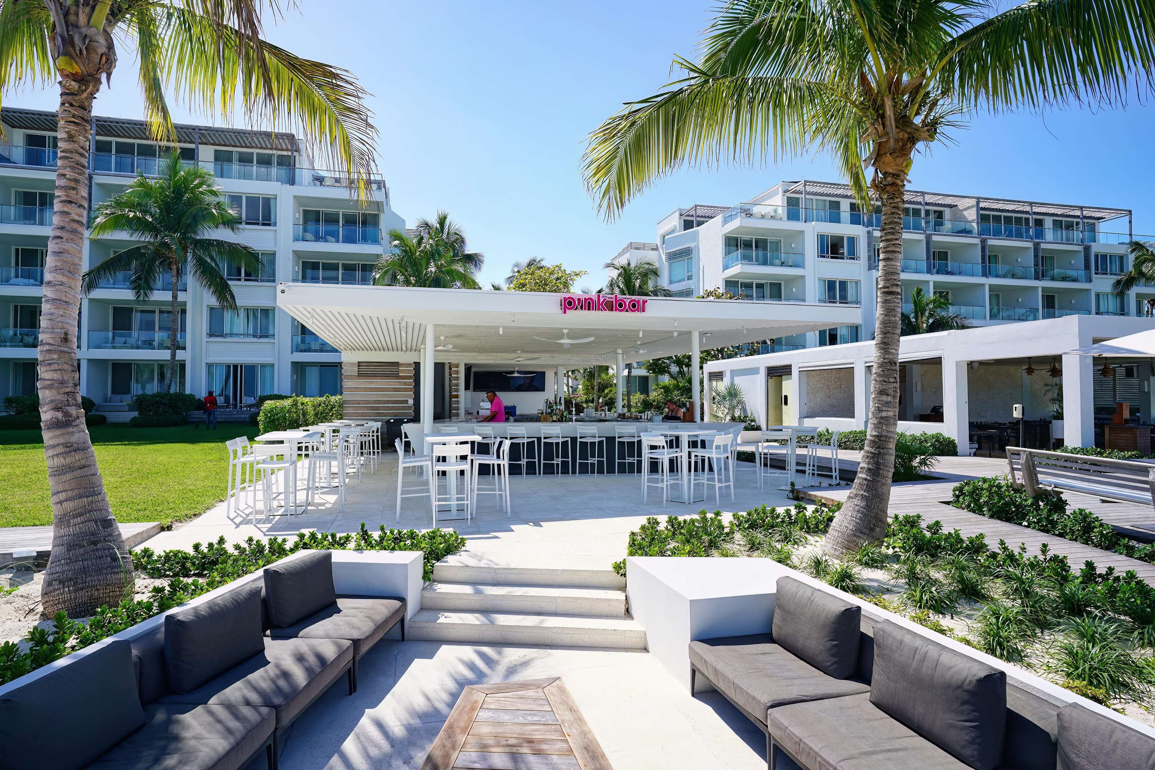 Uma área de bar moderna ao ar livre, com assentos e vista para a piscina e o edifício do hotel.
