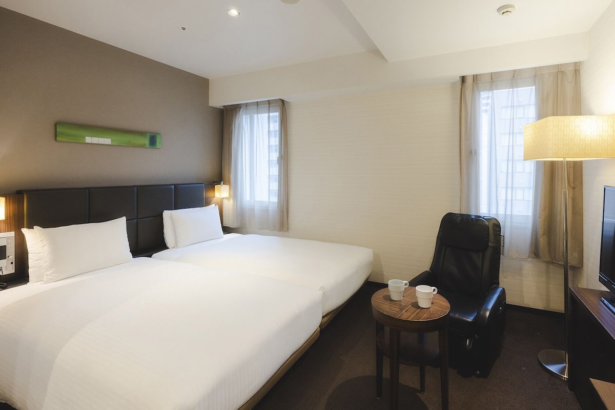 Quarto de hotel com uma cama grande, uma escrivaninha com cadeira, uma televisão e um abajur.