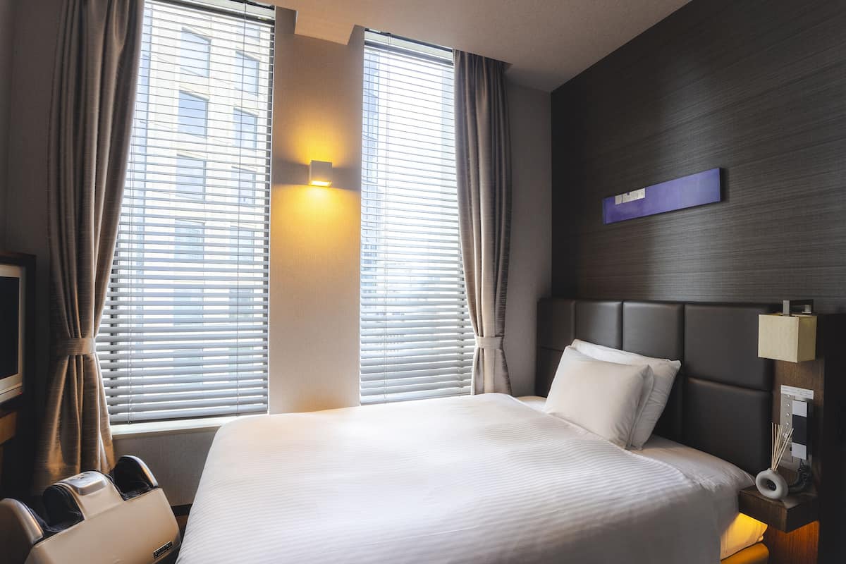 Quarto de hotel com cama grande, televisão, cadeira de massagem e luz embutida na parede.