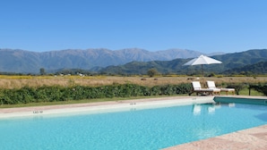 Uma piscina com espreguiçadeiras e um guarda-sol, cercada por montanhas.