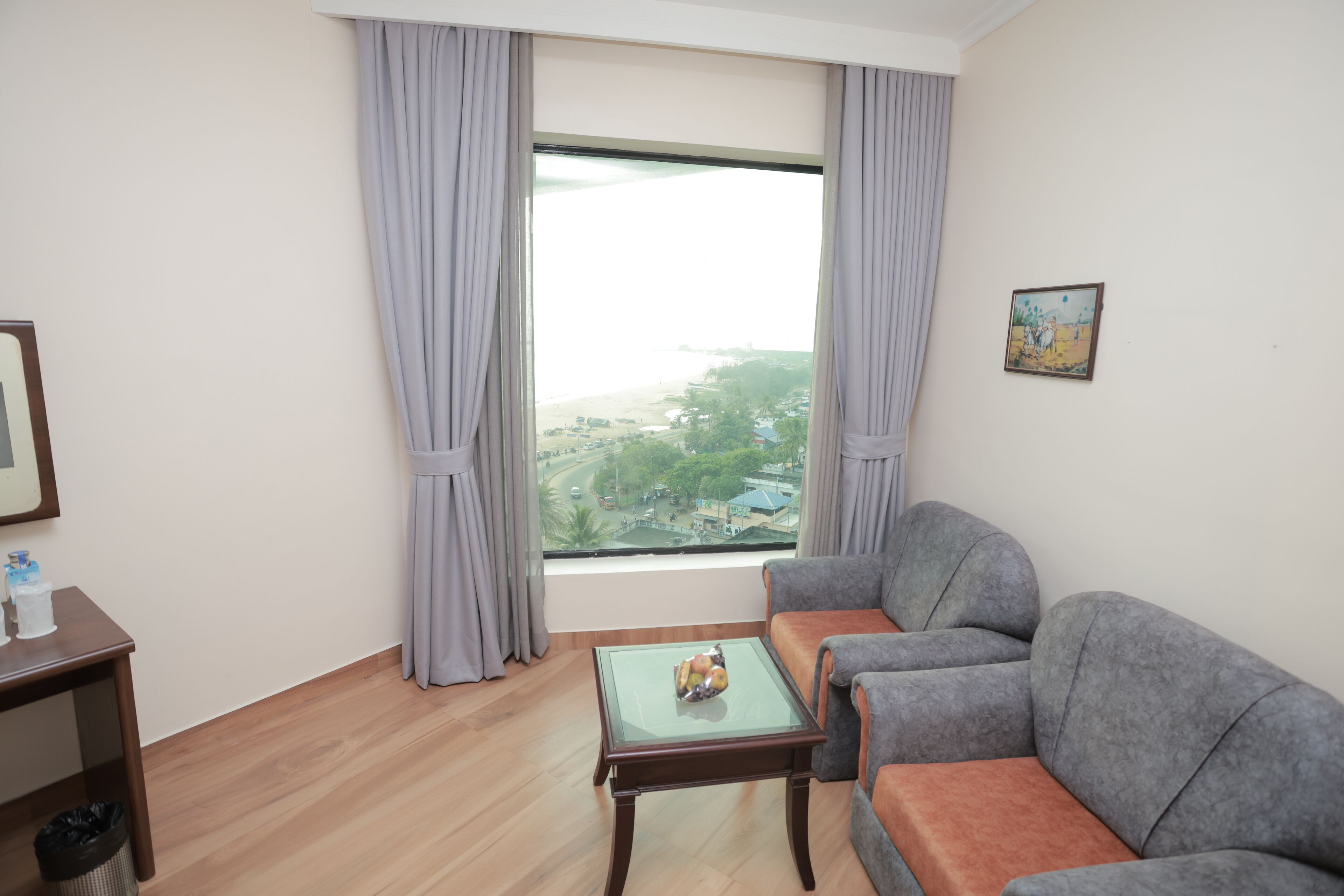 Sala de estar com sofá, mesa de centro de vidro e vista para o horizonte urbano através de uma grande janela com cortinas.