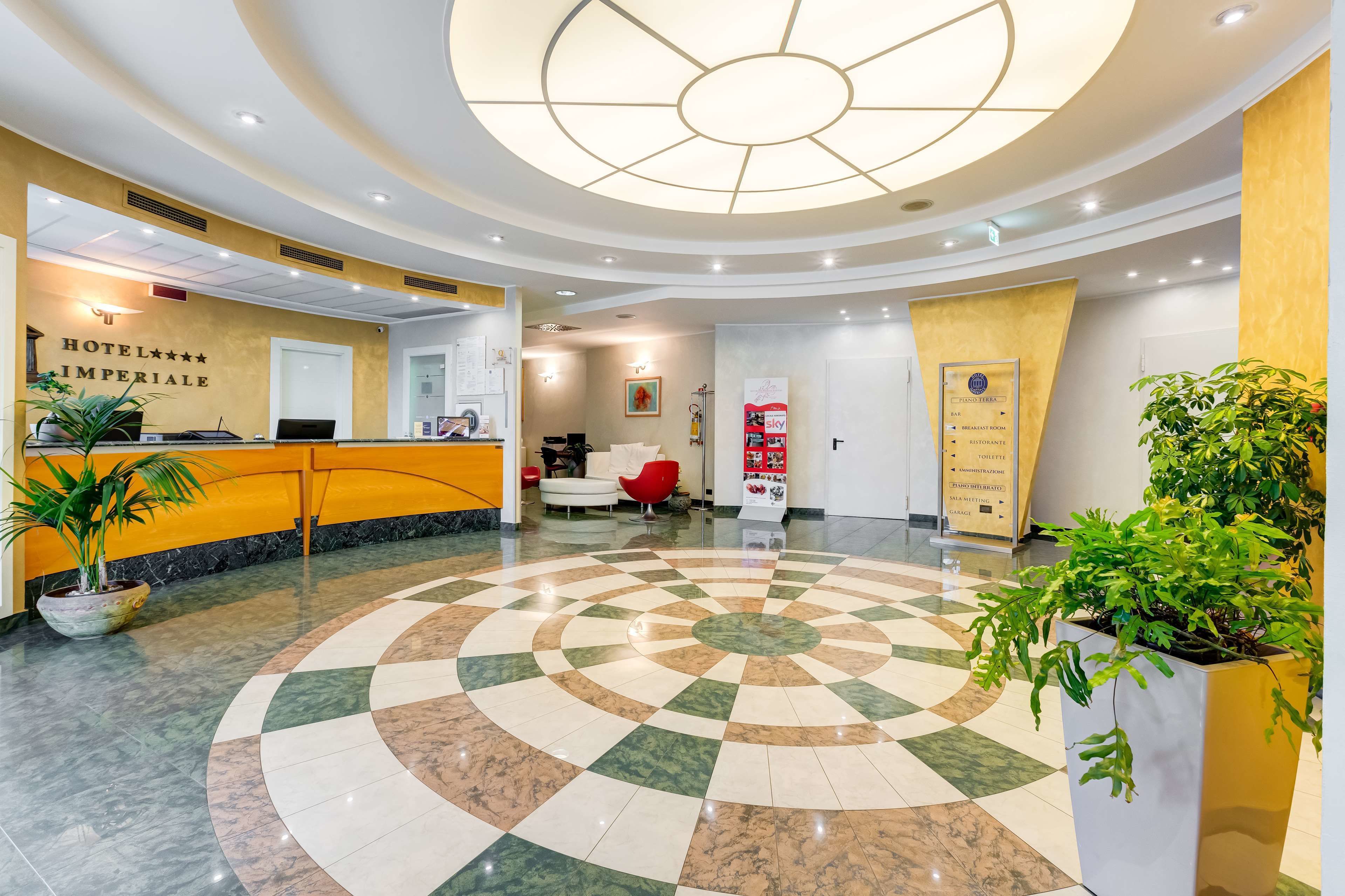 Um saguão de hotel com balcão de recepção, balcão de check-in, área de estar e um desenho decorativo no chão.