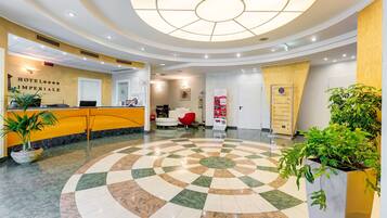 Um saguão de hotel com balcão de recepção, balcão de check-in, área de estar e um desenho decorativo no chão.