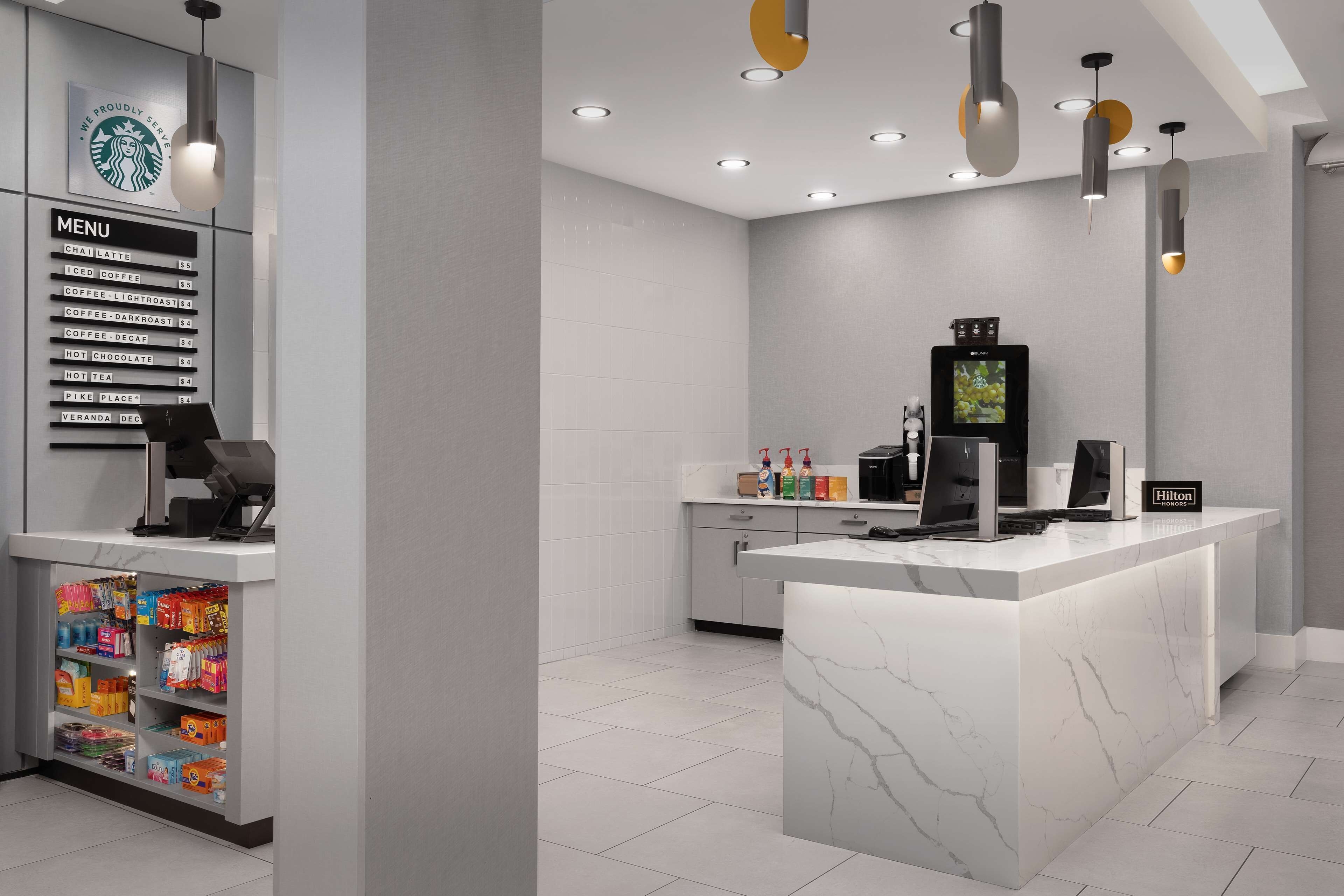 Um lobby de hotel moderno com um balcão da Starbucks, um cardápio, um minibar e uma mesa de recepção.