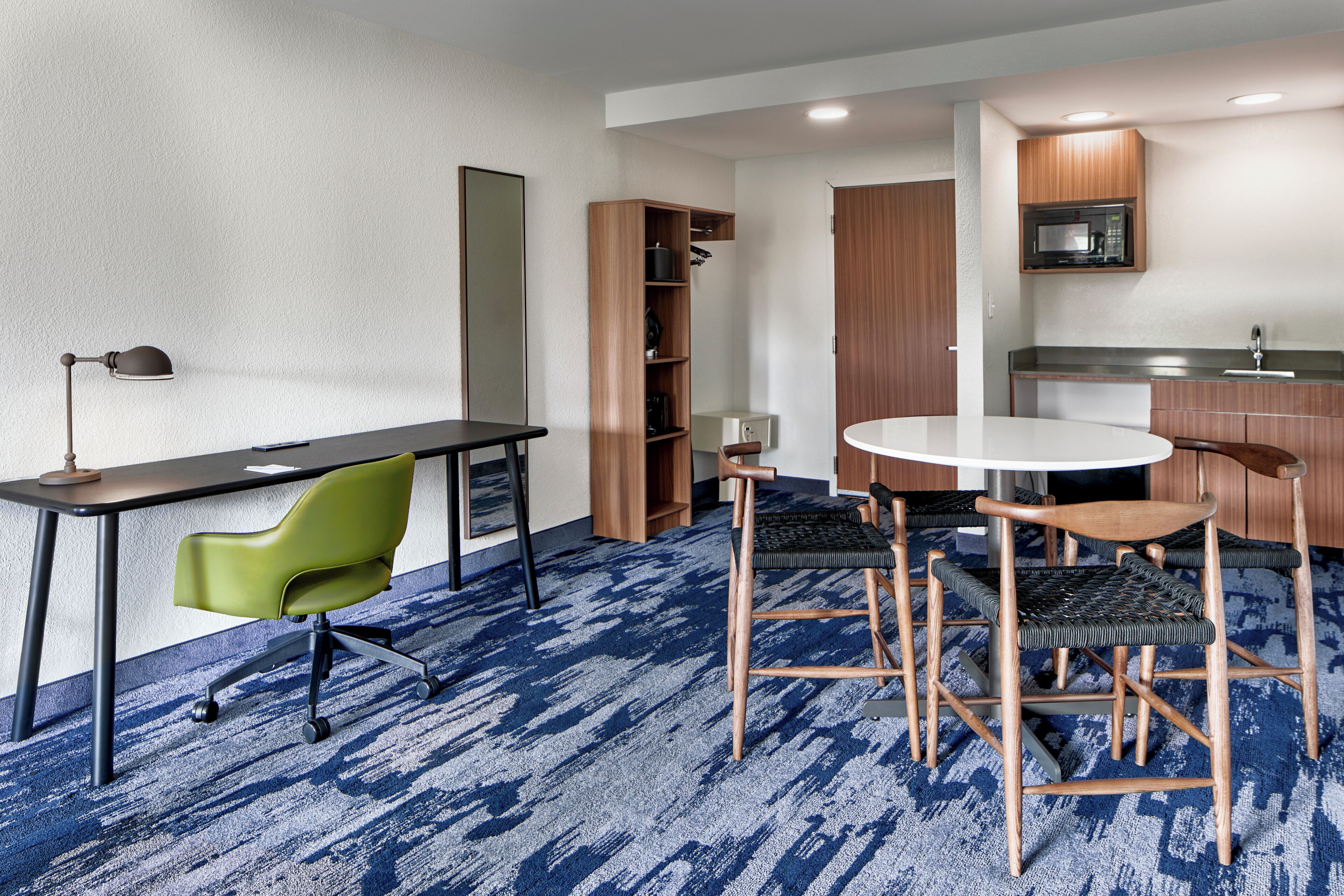 Quarto de hotel com escrivaninha, cadeiras, mesa redonda, estante, micro-ondas e armário.