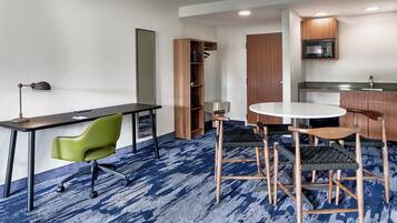 Quarto de hotel com escrivaninha, cadeiras, mesa redonda, estante, micro-ondas e armário.