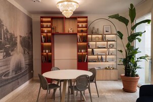 Uma sala de jantar com uma mesa redonda e cadeiras, rodeada por estantes de livros e um vaso grande com planta.