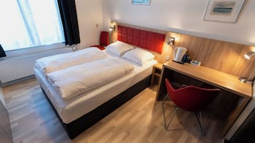 Quarto de hotel com uma cama de casal, uma escrivaninha com cadeira, uma cafeteira e um quadro na parede.
