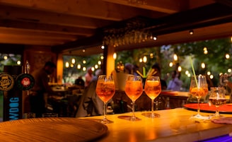 Uma área de bar com mesas de madeira e copos de bebidas âmbar.