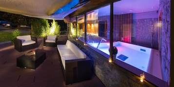 Área de spa ao ar livre com hidromassagem, assentos e parede de pedra.