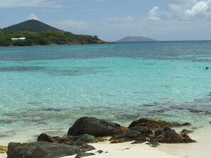 Uma praia com águas turquesa cristalinas, costa rochosa e uma montanha ao longe.