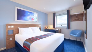 Quarto de hotel com cama grande, escrivaninha, cadeira, televisão e janela com cortinas.