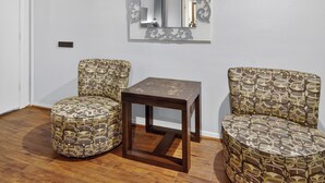 Um quarto com duas poltronas estampadas, uma mesa de madeira pequena e um espelho na parede.