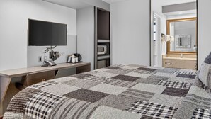 Quarto de hotel moderno com uma cama grande, uma mesa de trabalho com TV de tela plana, micro-ondas e uma pequena cozinha equipada.