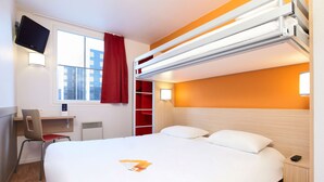 Quarto de hotel com uma cama, uma escrivaninha com cadeira, uma televisão na parede e uma janela com cortinas vermelhas.