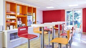 Uma cafeteria bem iluminada com esquema de cores laranja e branco, com várias mesas e cadeiras, e uma grande janela que oferece vista para o exterior.