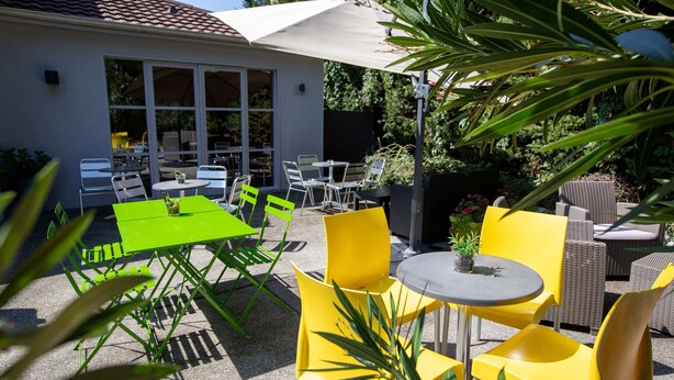 Uma área de pátio ao ar livre com cadeiras amarelas e verdes, uma mesa e um espaço de estar coberto.