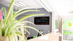 Uma área de recepção com um quadro negro exibindo uma frase, um balcão de atendimento e uma parede verde.
