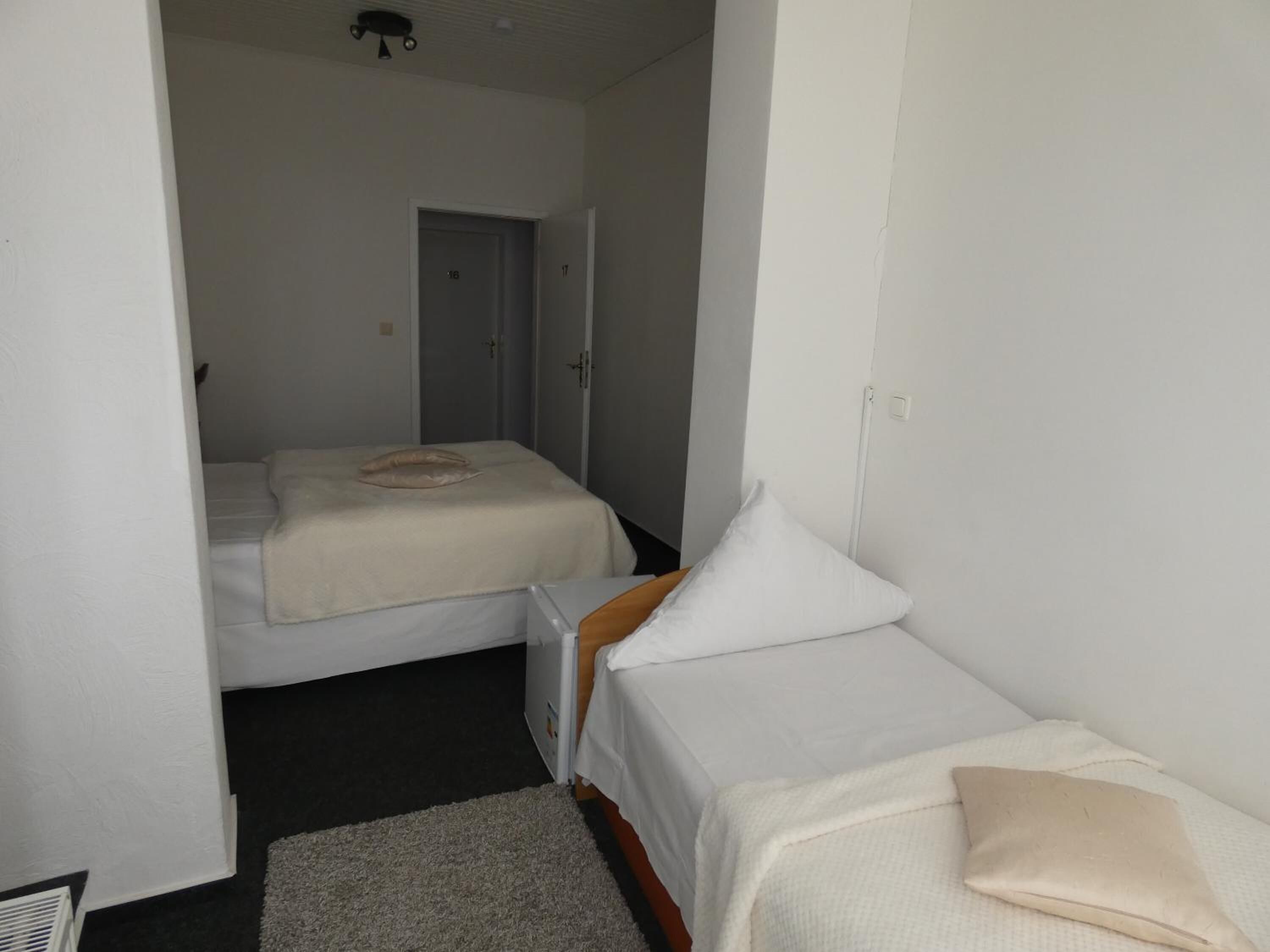 Quarto de hotel pequeno e individual com duas camas, uma porta e piso coberto de carpete.
