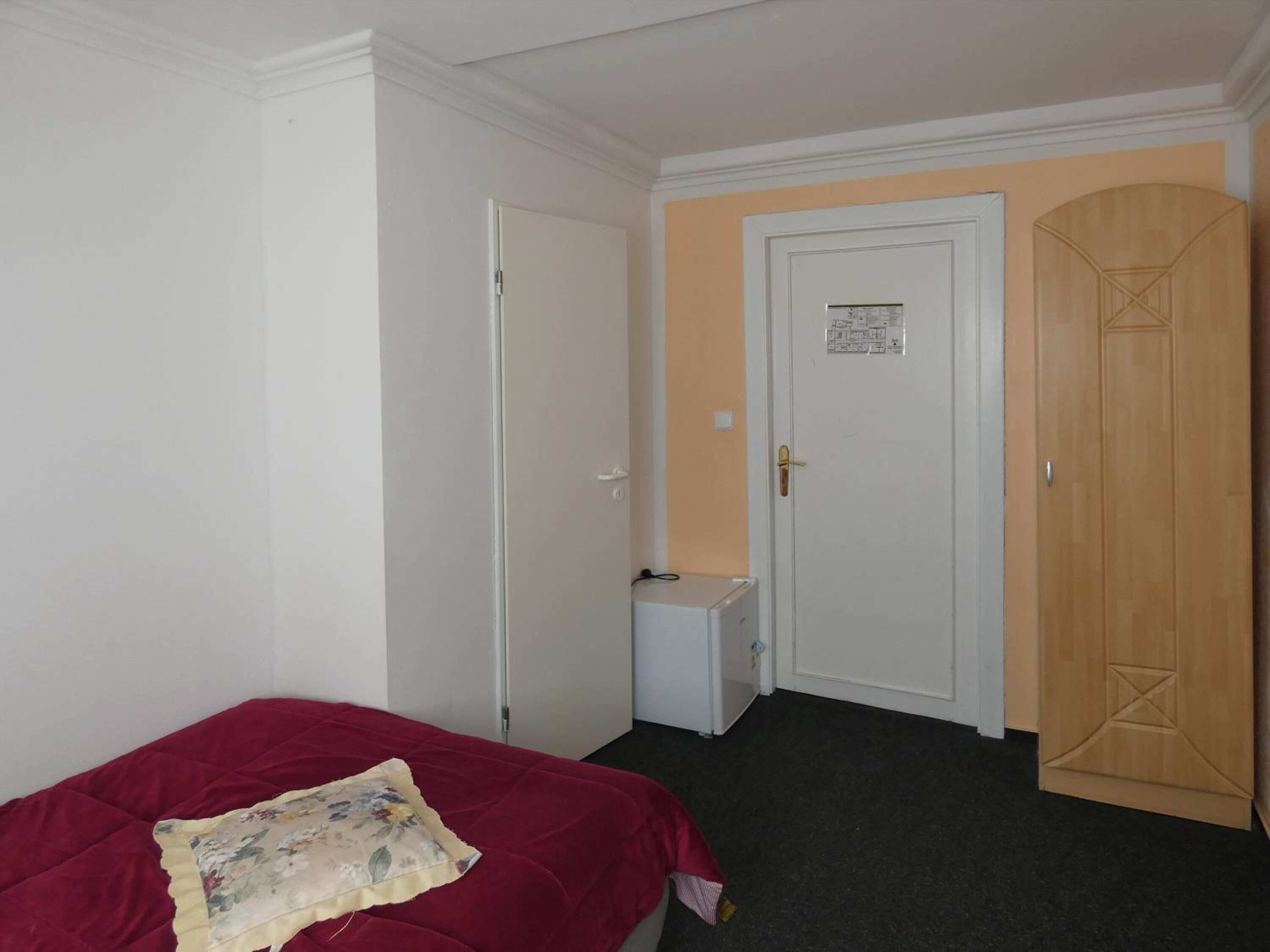 Quarto com cama, guarda-roupa, porta com aviso e mesa de cabeceira pequena.