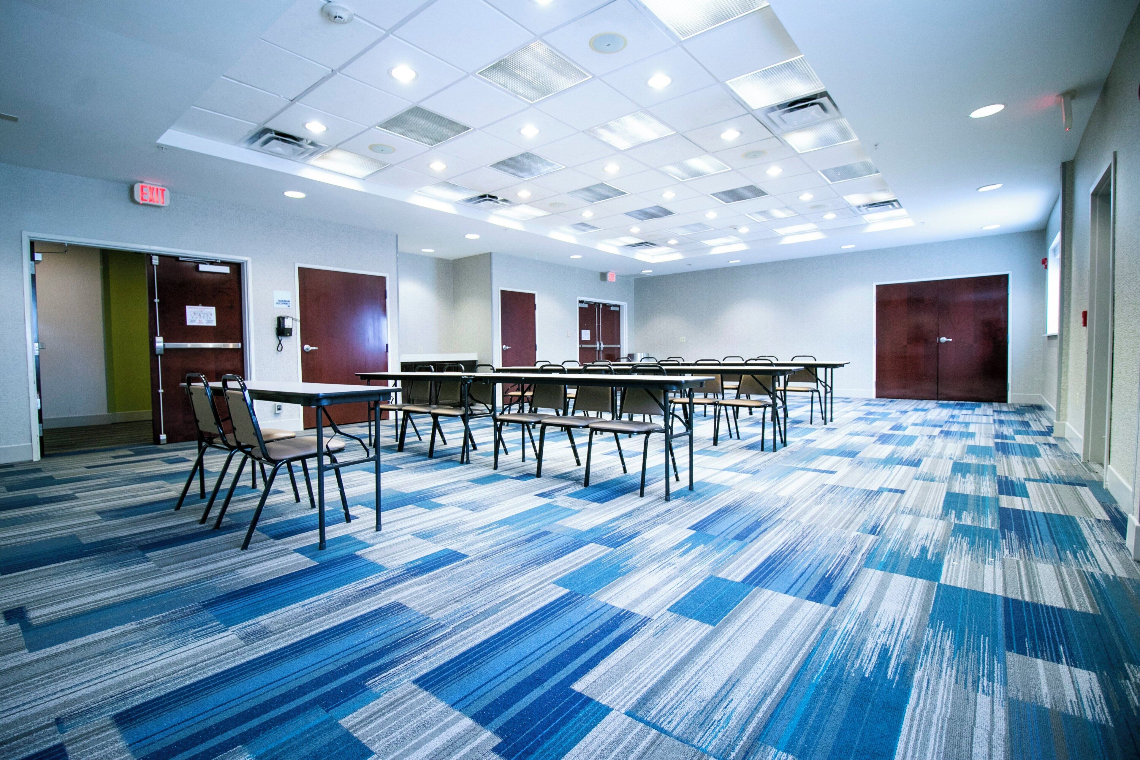 Uma sala de conferências com várias mesas e cadeiras, um tapete estampado e algumas portas.