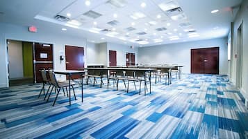 Uma sala de conferências com várias mesas e cadeiras, um tapete estampado e algumas portas.