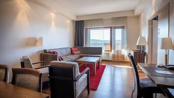Uma sala de estar moderna com sofá, mesa de centro e cadeiras. Há também um espaço de jantar com mesa e cadeiras. O ambiente possui janelas amplas com cortinas e vista para o exterior.